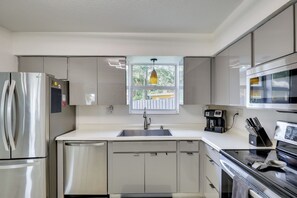 Uma cozinha moderna com eletrodomésticos de aço inoxidável, lava-louças embutida e janela com vista para palmeiras.