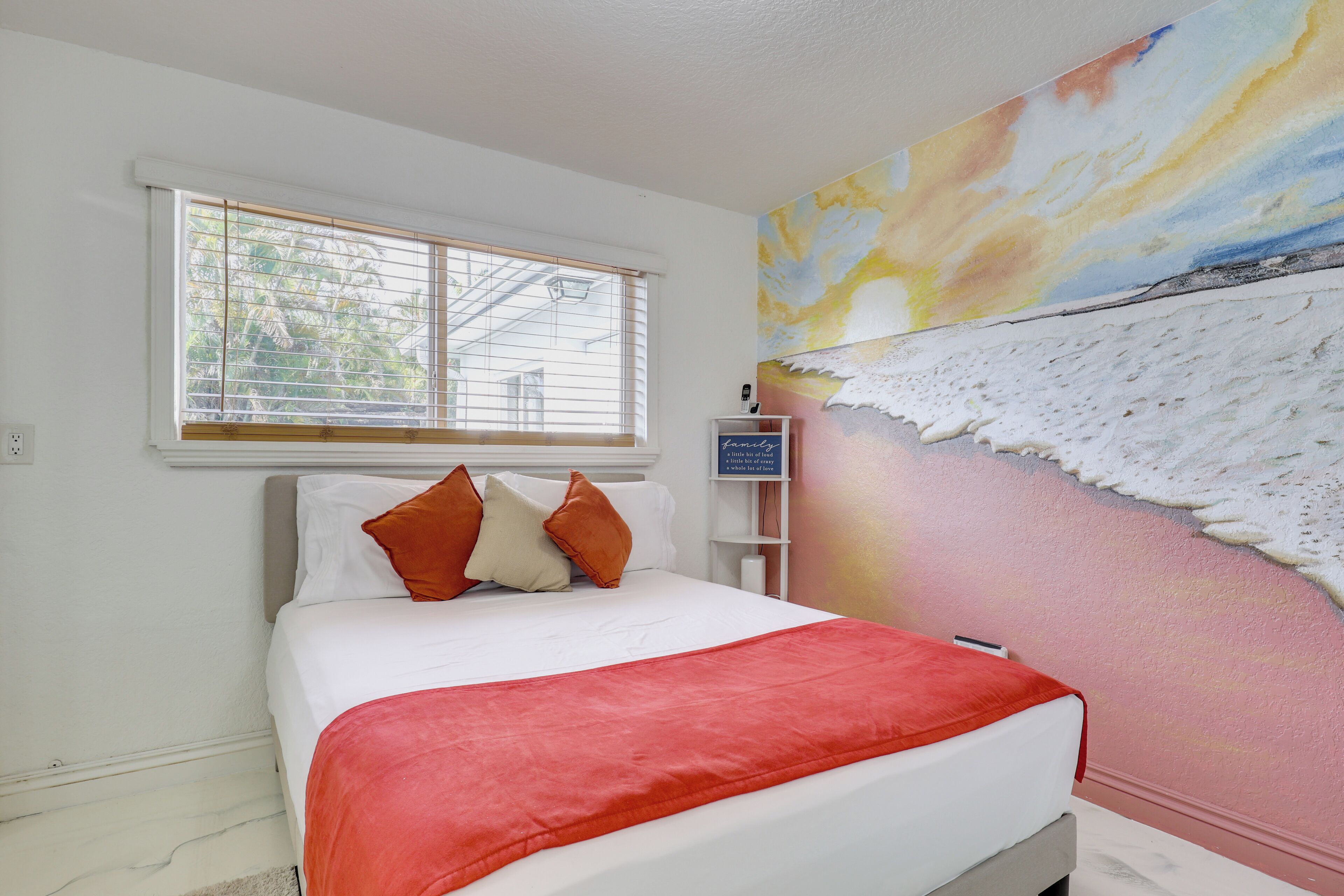 Quarto com cama, janela, parede com pintura parcial e prateleira com telefone.