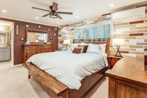 Quarto com cama de madeira, mesa de cabeceira, cômoda, ventoinha no teto e parede com padrão de tijolos.