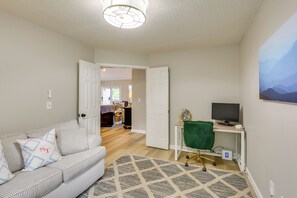 Uma sala de estar com um sofá, uma escrivaninha com computador, uma cadeira verde e um quadro na parede.