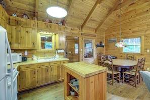 Interior de uma cabana de madeira com cozinha, área de jantar e uma janela grande com vista.