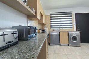 Uma cozinha com torradeira, micro-ondas, lava-louças e uma janela com persianas.