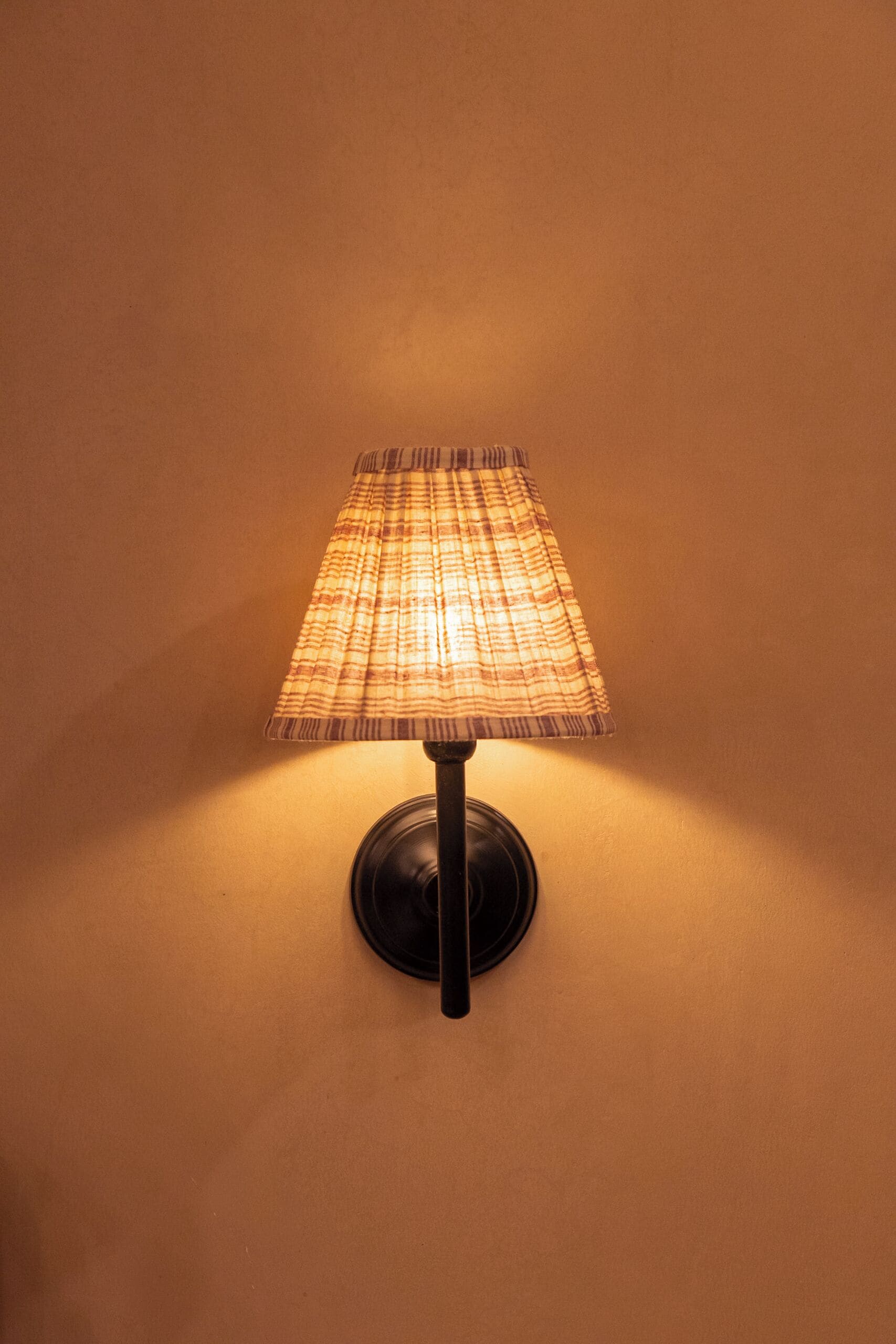 Um abajur com cúpula xadrez sobre uma parede lisa.