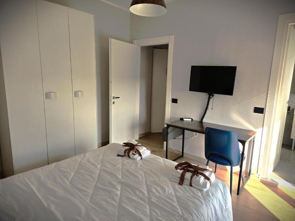 Quarto de hotel com cama, escrivaninha, cadeira, televisão e guarda-roupa.