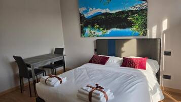 Quarto de hotel com uma cama, uma escrivaninha e um quadro de um lago.