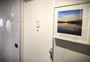 Uma porta com o número '3' e um quadro emoldurado mostrando um pôr do sol sobre a água, com a palavra 'VIVERONE' abaixo.