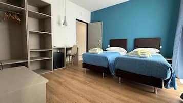 Quarto de hotel com duas camas, uma escrivaninha e um guarda-roupa.