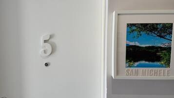 Paredes brancas com o número '5' e um quadro emoldurado com a inscrição 'SAN MICHELE' à direita.