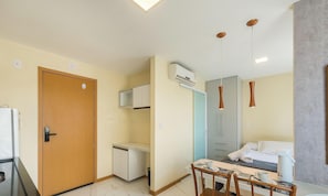 Quarto de hotel com cama, escrivaninha com cadeira, pequeno espaço de cozinha, guarda-roupa e banheiro.