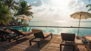 Um deck de madeira com espreguiçadeiras e guarda-sóis com vista para a piscina e o oceano.