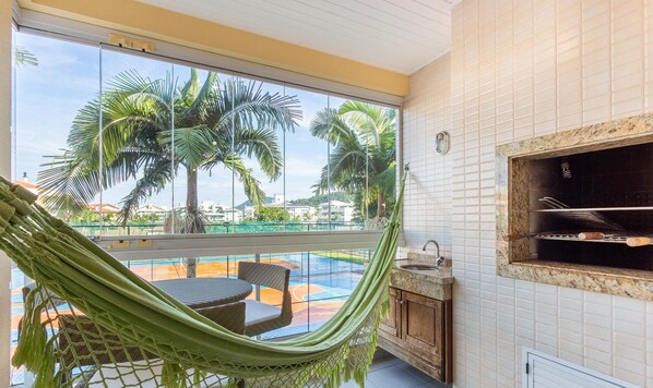 Uma varanda com rede, piscina e vista para palmeiras.