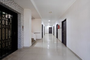 Um corredor comprido e estreito, com parede revestida de azulejos de um lado, escada com corrimão e portas do outro.