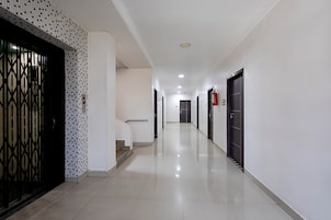 Um corredor comprido e estreito, com parede revestida de azulejos de um lado, escada com corrimão e portas do outro.