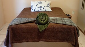 Uma cama com um cobertor marrom, um travesseiro branco com desenho floral e uma toalha verde sobre a cama.