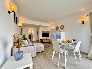 Uma sala de estar moderna com sofá, mesa de jantar, cadeiras, televisão e luminárias decorativas na parede.