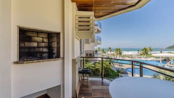 Uma varanda com vista para uma piscina e praia, uma mesa pequena e uma janela com grade.