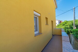 Um edifício amarelo com uma pequena janela e uma porta, um caminho de azulejos e uma parede de pedra.