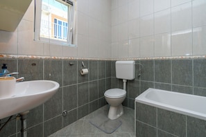 Casa de banho com lavatório, sanita e banheira, revestida a azulejos num padrão uniforme.