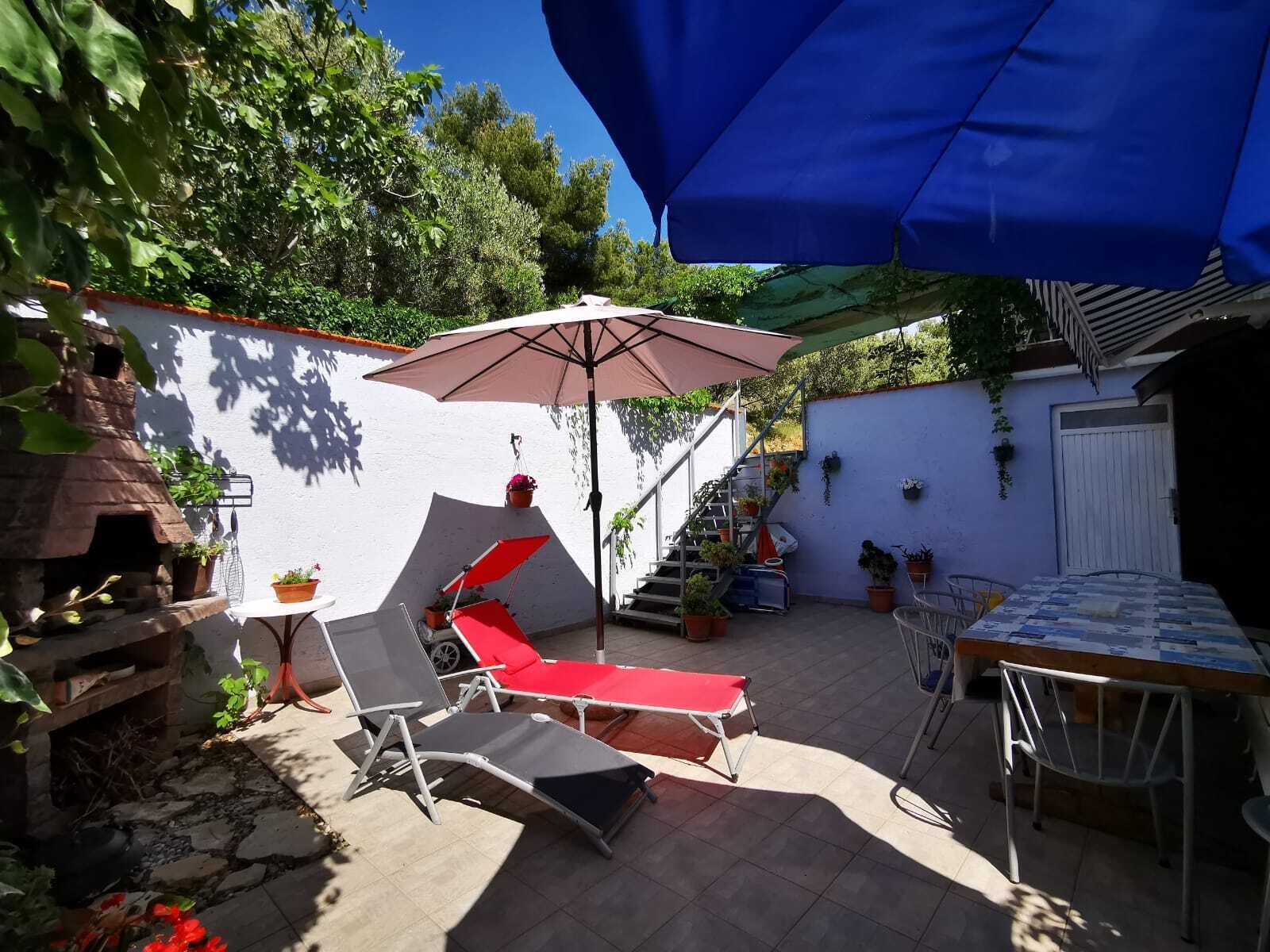 Um pátio com duas cadeiras de estar, uma mesa e um guarda-sol azul.