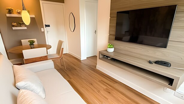 Uma sala de estar moderna com um sofá, uma mesa de jantar com cadeiras, uma TV fixada em uma parede de madeira, e uma porta com uma cruz.