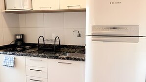 Uma cozinha com armários brancos, uma geladeira de aço inoxidável, uma cafeteira e uma pia.