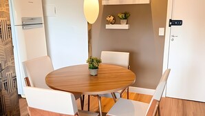 Uma sala de jantar com uma mesa redonda, quatro cadeiras, um vaso de planta e uma geladeira.