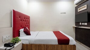 Quarto com cabeceira estofada vermelha, colcha branca, manta vermelha, televisão montada na parede e ar condicionado fixado na parede.