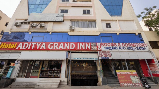 Um hotel com placas indicando 'Hotel Aditya Grand Inn' e 'Quartos & Quartos de Luxo'.