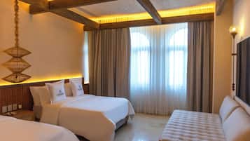 Quarto de hotel com duas camas, um sofá, um candeeiro pendente e uma janela grande com cortinas.