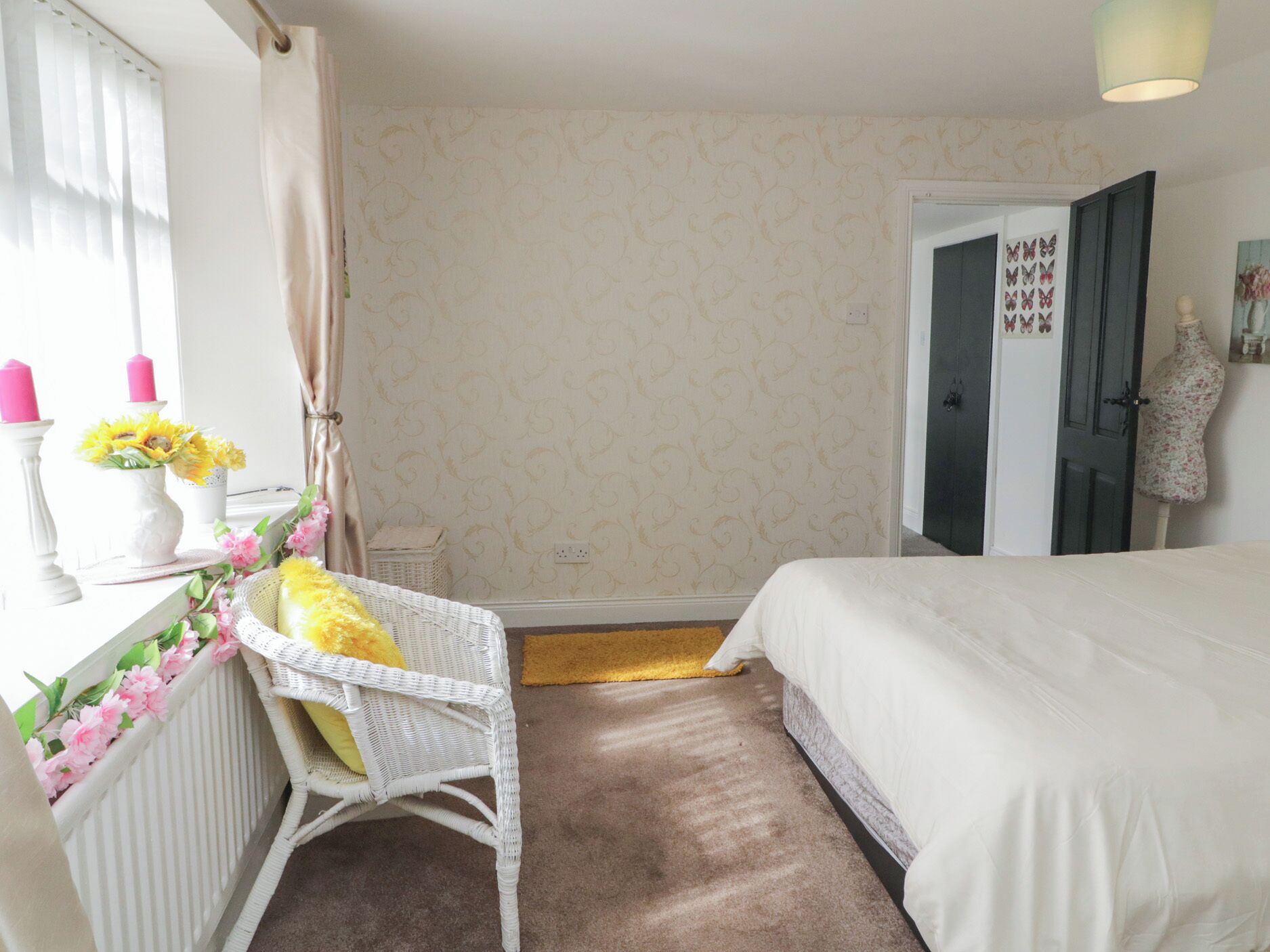 Um quarto com cama, uma cadeira, uma janela com cortinas e uma porta.