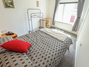Um quarto com cama, escrivaninha, cadeira e radiador.
