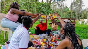 Um grupo de pessoas sentadas ao ar livre com comida e bebidas, rodeadas por vegetação.