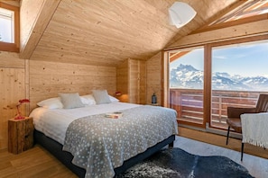 Quarto de cabana de madeira com uma cama, mesa de cabeceira, cadeira e vista para as montanhas.
