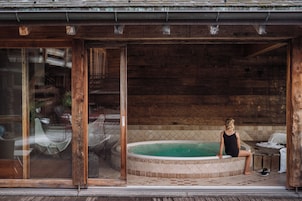 Uma cabana de madeira com porta de vidro que dá para uma área com hidromassagem.