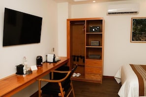 Quarto de hotel com escrivaninha de madeira, televisão, armário e uma cama.
