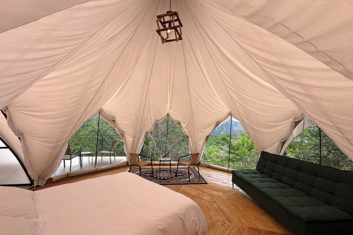 Acomodação em tenda com cama, sofá e vista para o exterior.
