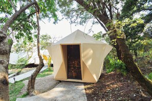 Uma pequena construção de um único cômodo com uma porta, cercada por árvores e um caminho de cascalho.