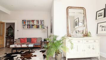 Uma sala de estar com um sofá branco, um tapete de couro de vaca, uma estante de livros, um armário branco e um espelho grande.