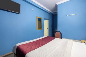 Quarto de hotel com uma cama de solteiro, uma janela pequena, uma porta e um espelho na parede.
