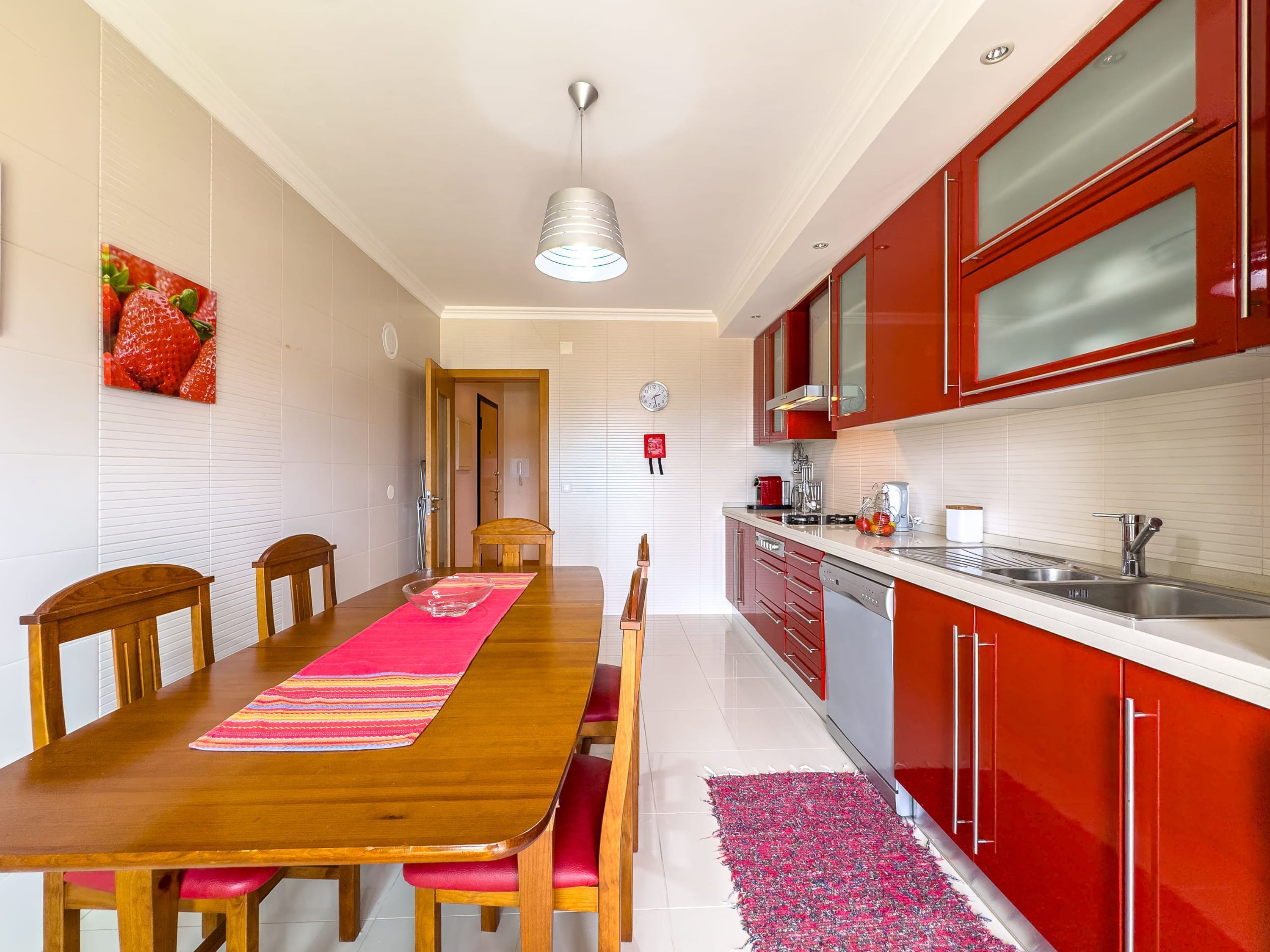 Uma cozinha moderna com armários vermelhos, uma pia de aço inoxidável e uma mesa de jantar de madeira com cadeiras.