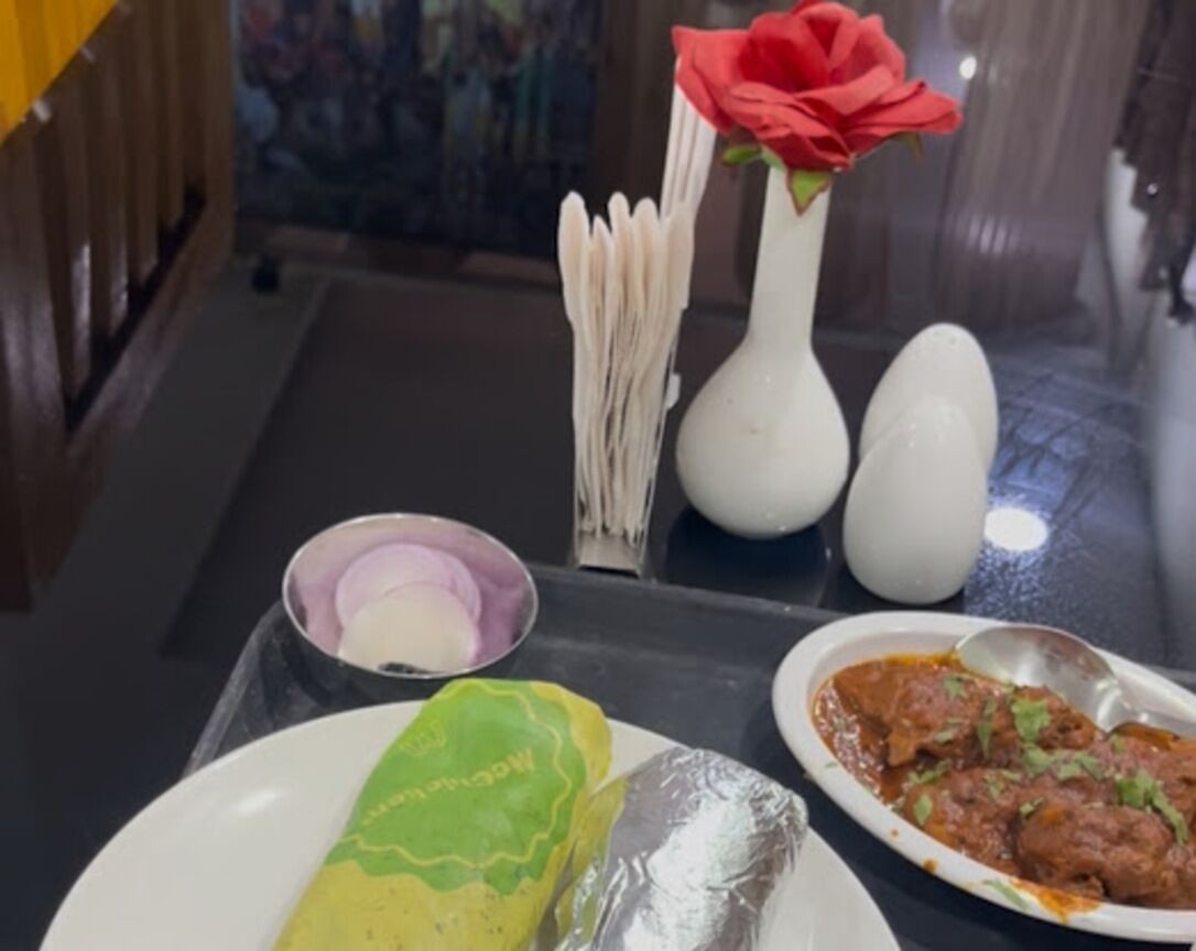 Uma mesa de jantar com um prato de comida, um vaso branco com uma flor vermelha e uma pequena tigela de acompanhamentos.