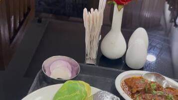 Uma mesa de jantar com um prato de comida, um vaso branco com uma flor vermelha e uma pequena tigela de acompanhamentos.