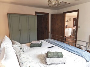 Quarto com cama, almofadas, cobertor, controle remoto e guarda-roupa.