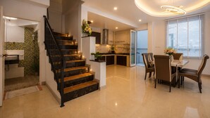 Uma cozinha moderna com uma ilha central, uma área de jantar com mesa e cadeiras, e uma escada que leva a um andar superior.