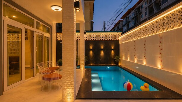 Uma piscina com deck revestido, uma cadeira e iluminação decorativa.