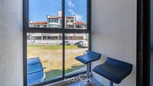 Uma janela com vista para um edifício, um estacionamento e duas cadeiras.