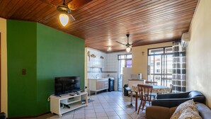 Uma sala de estar com televisão, sofá e um espaço de jantar com cadeiras e mesa.