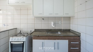 Cozinha com armários brancos, fogão a gás, pia e bancada de madeira.