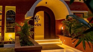Entrada de hotel com fachada de tijolos, arco iluminado em amarelo e placa com o nome do hotel.