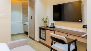 Quarto de hotel moderno com sofá, escrivaninha com cadeira, televisão de tela plana e uma pequena planta.
